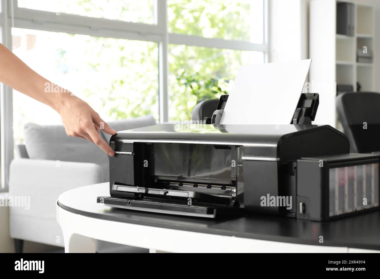 Female hands putting paper sheet in modern printer on table in stylish ...