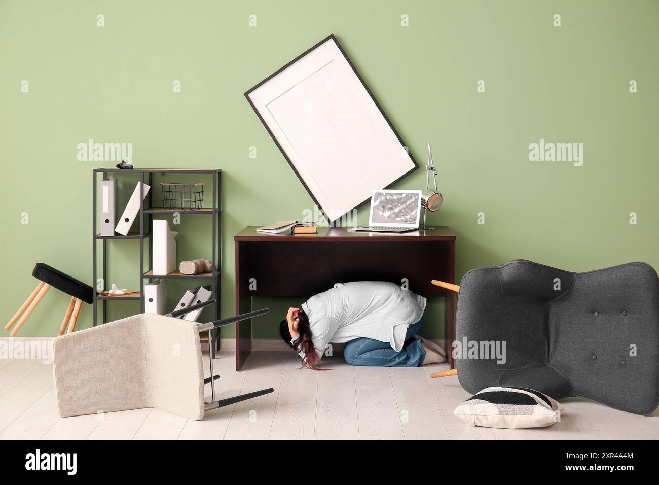 Young woman hiding under workplace in damaged office after earthquake ...