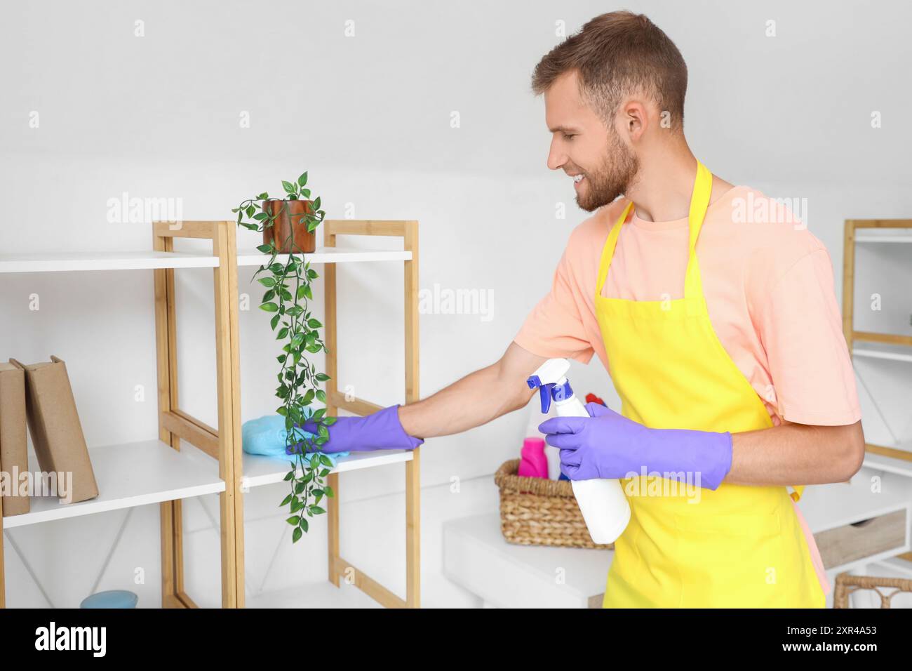 Male janitor cleaning shelving unit with rug and spray in room Stock ...
