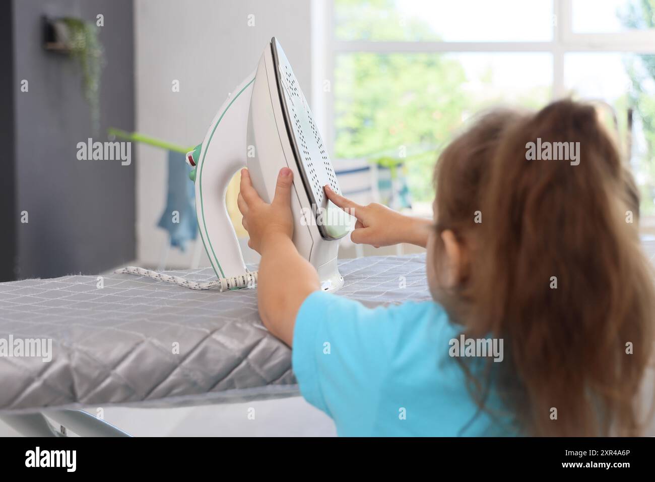 Cute little girl touching iron on board in bathroom, back view. Child ...