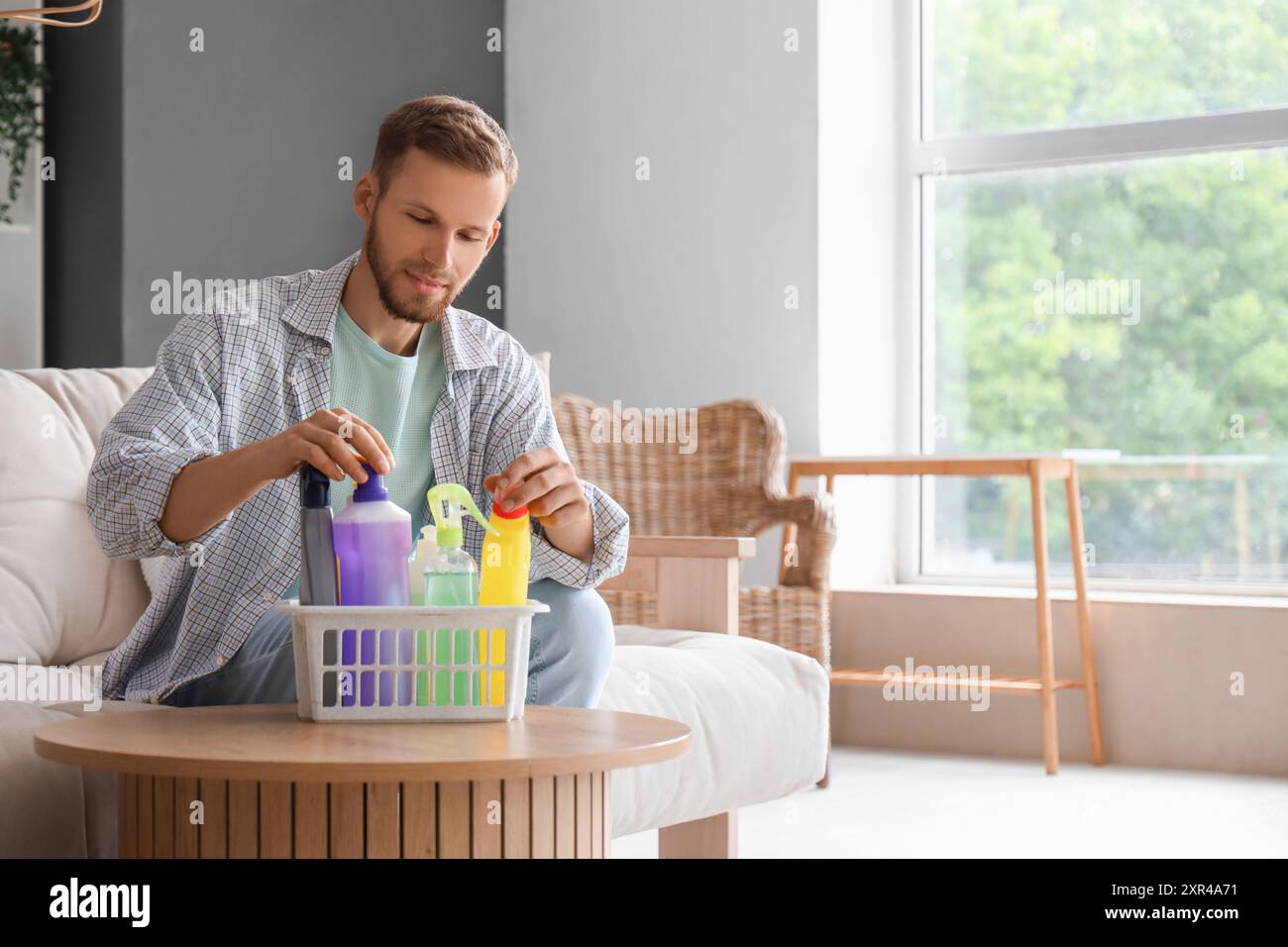 Male janitor and basket of cleaning supplies on coffee table in room ...