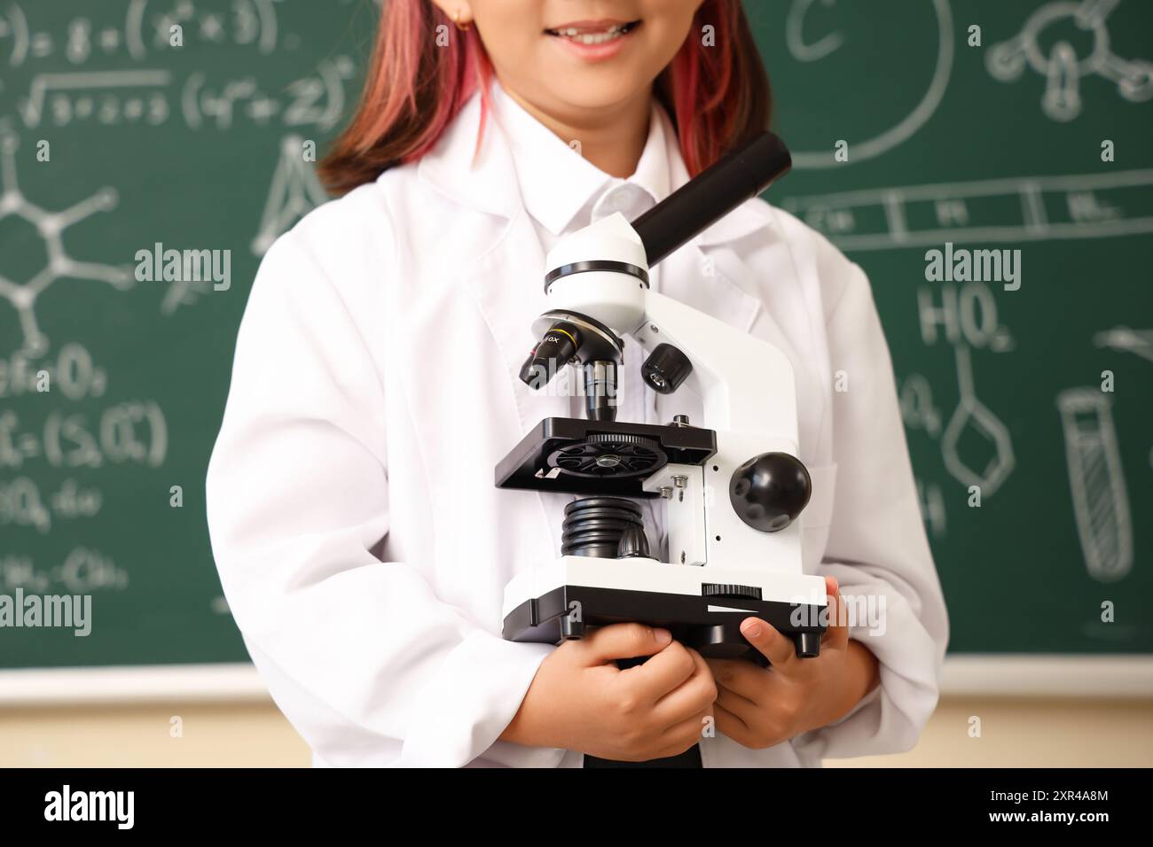 Cute little girl with microscope near chalkboard at chemistry lesson in ...