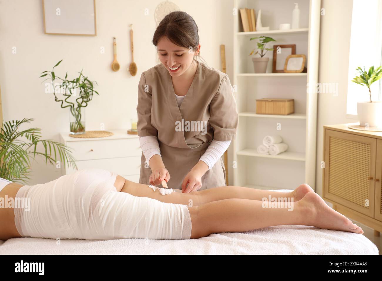 Massage therapist applying butter on woman's leg during bandage wrap ...
