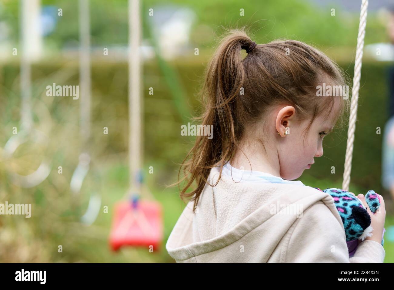 Little sad girl on swing in backyard in summer. Child loneliness ...