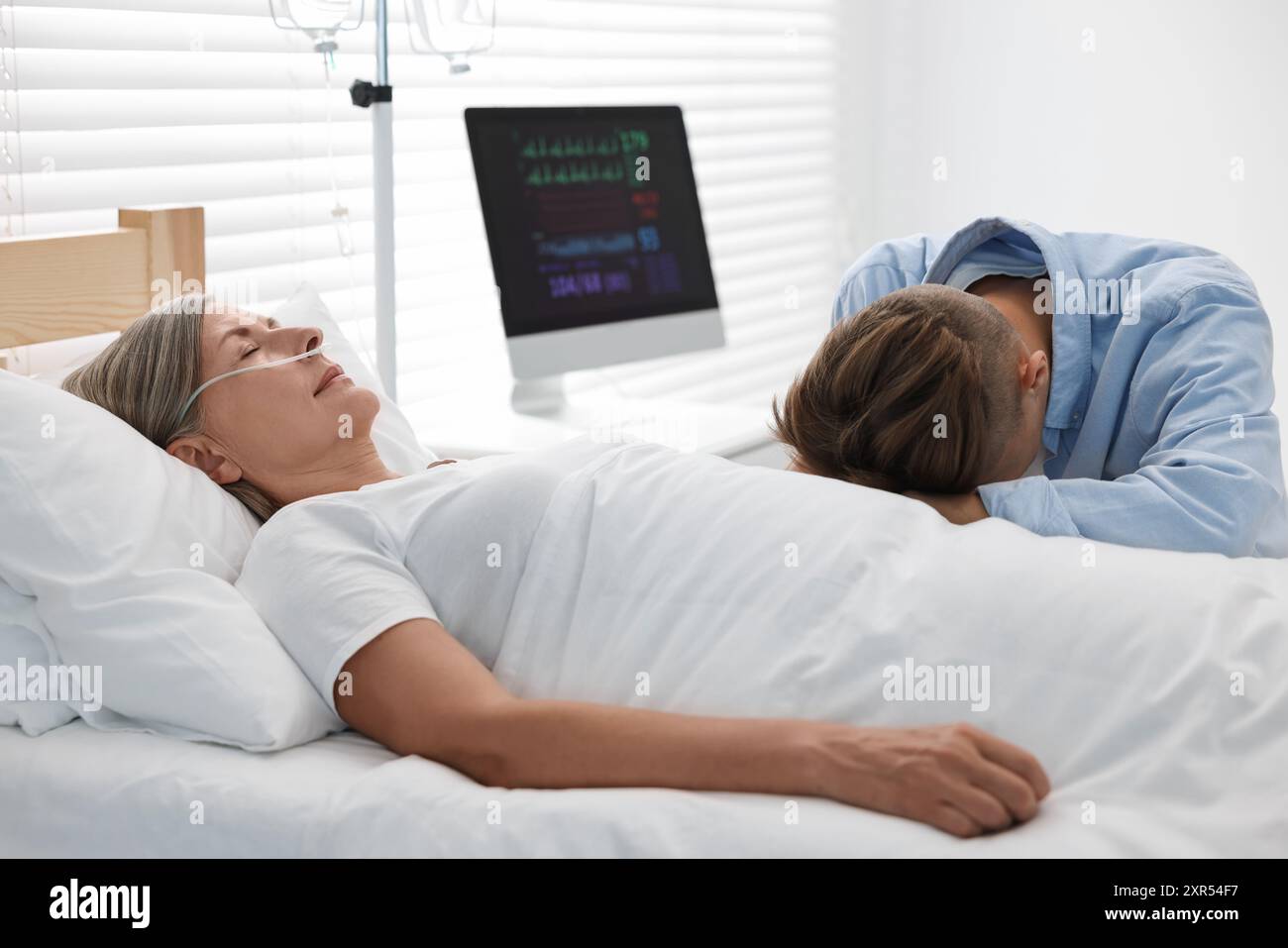 Coma patient. Sad young man near his unconscious mother in hospital ...