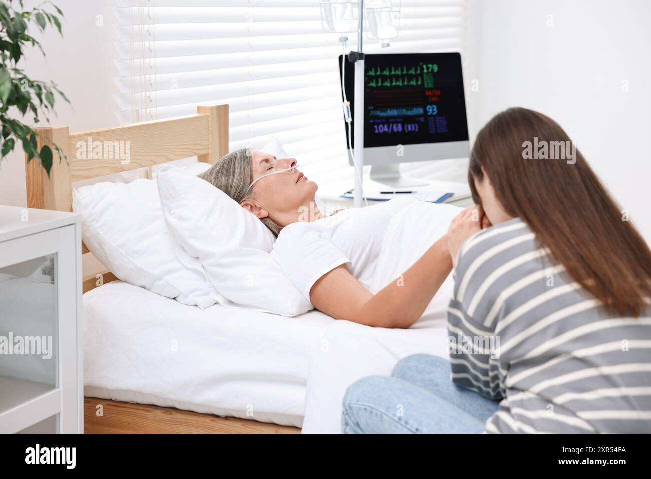Coma patient. Sad young woman near her unconscious mother in hospital ...