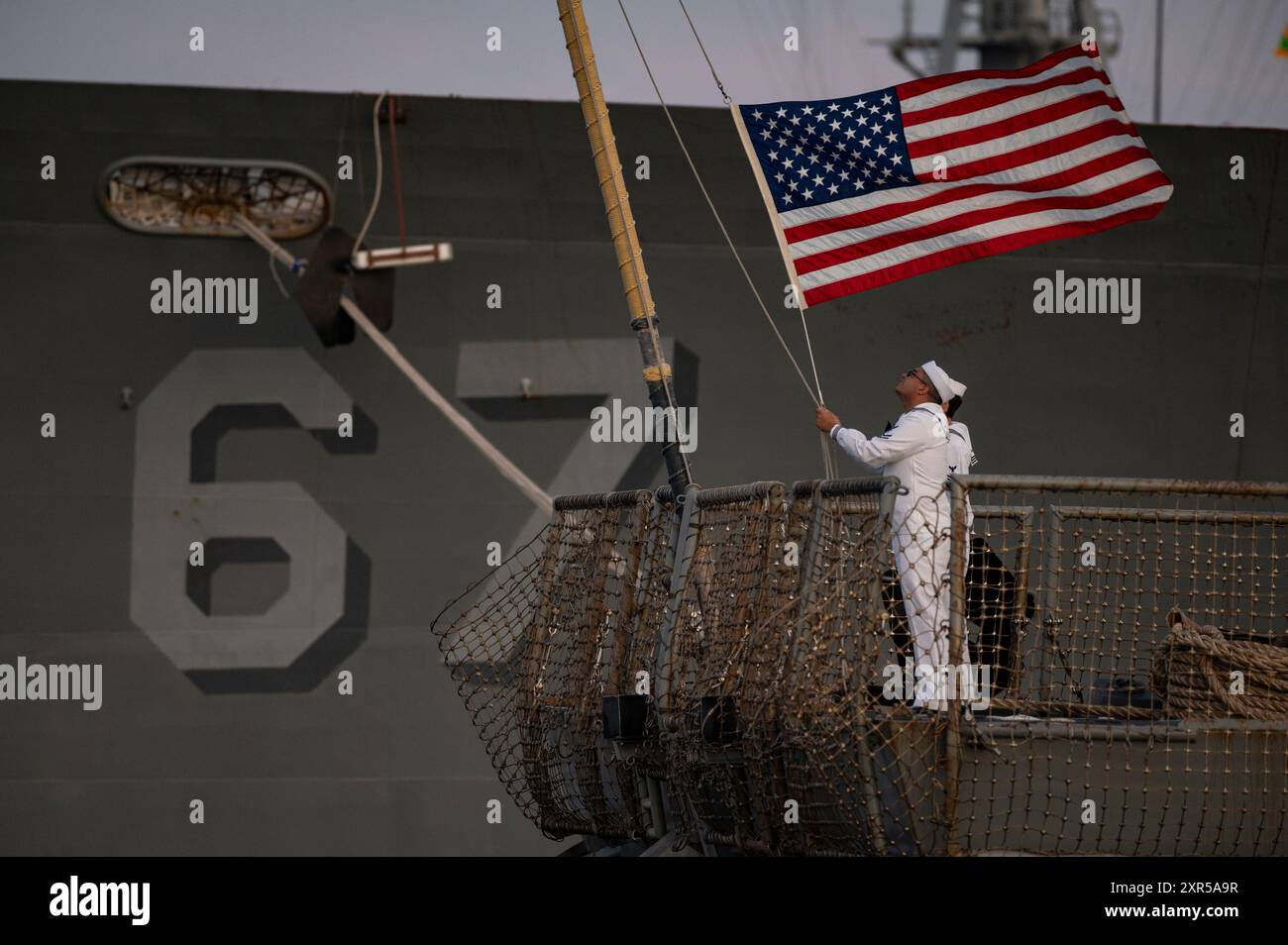 Sailors aboard the USS Wayne E. Meyer (DDG 108) lower the flag ...
