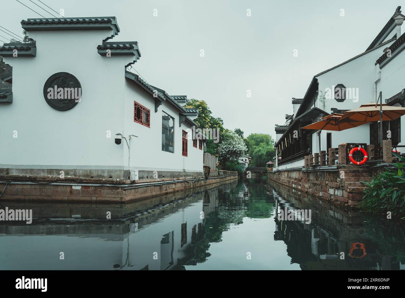 A narrow canal in Suzhou, China runs between two white buildings with ...