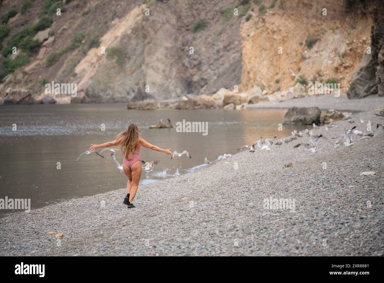 A woman is walking on a beach with a flock of seagulls flying around ...