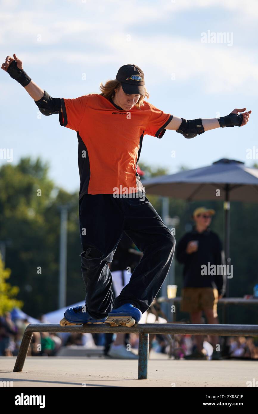 Teen roller blader performing sweat stance trick on a rail in skatepark ...