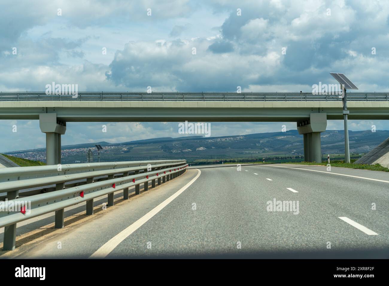 A bridge spans a road with a clear sky above. The bridge is a large ...