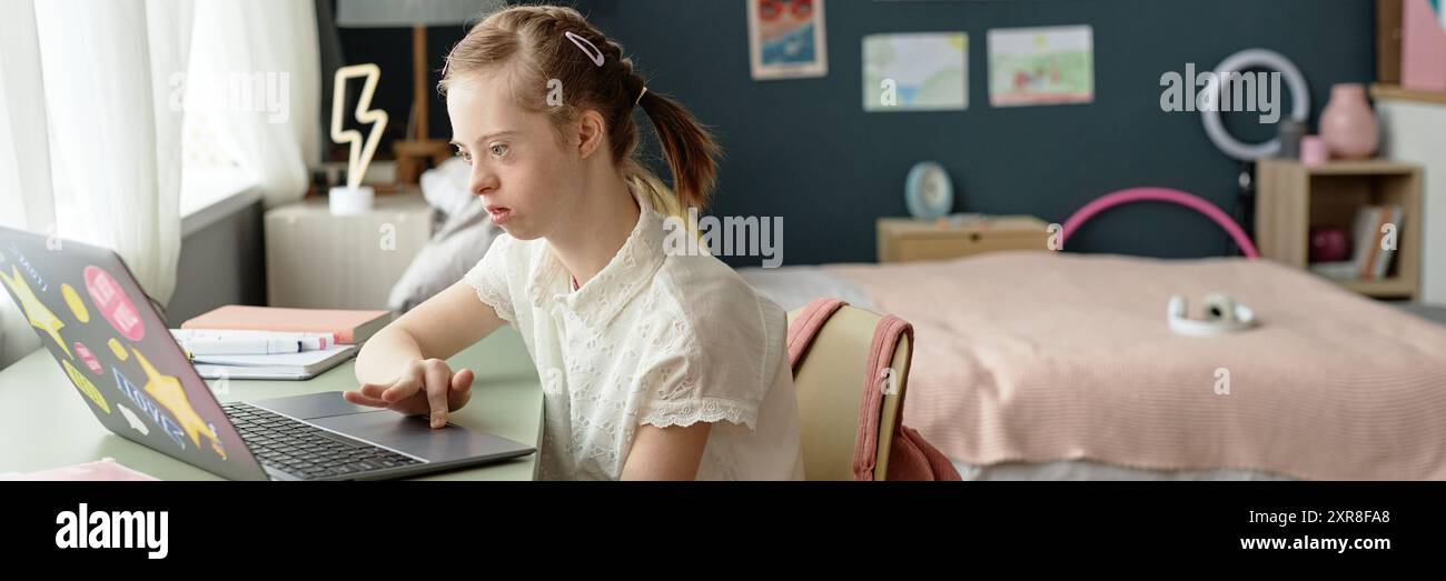 Side view of young girl with Down syndrome using laptop while studying ...
