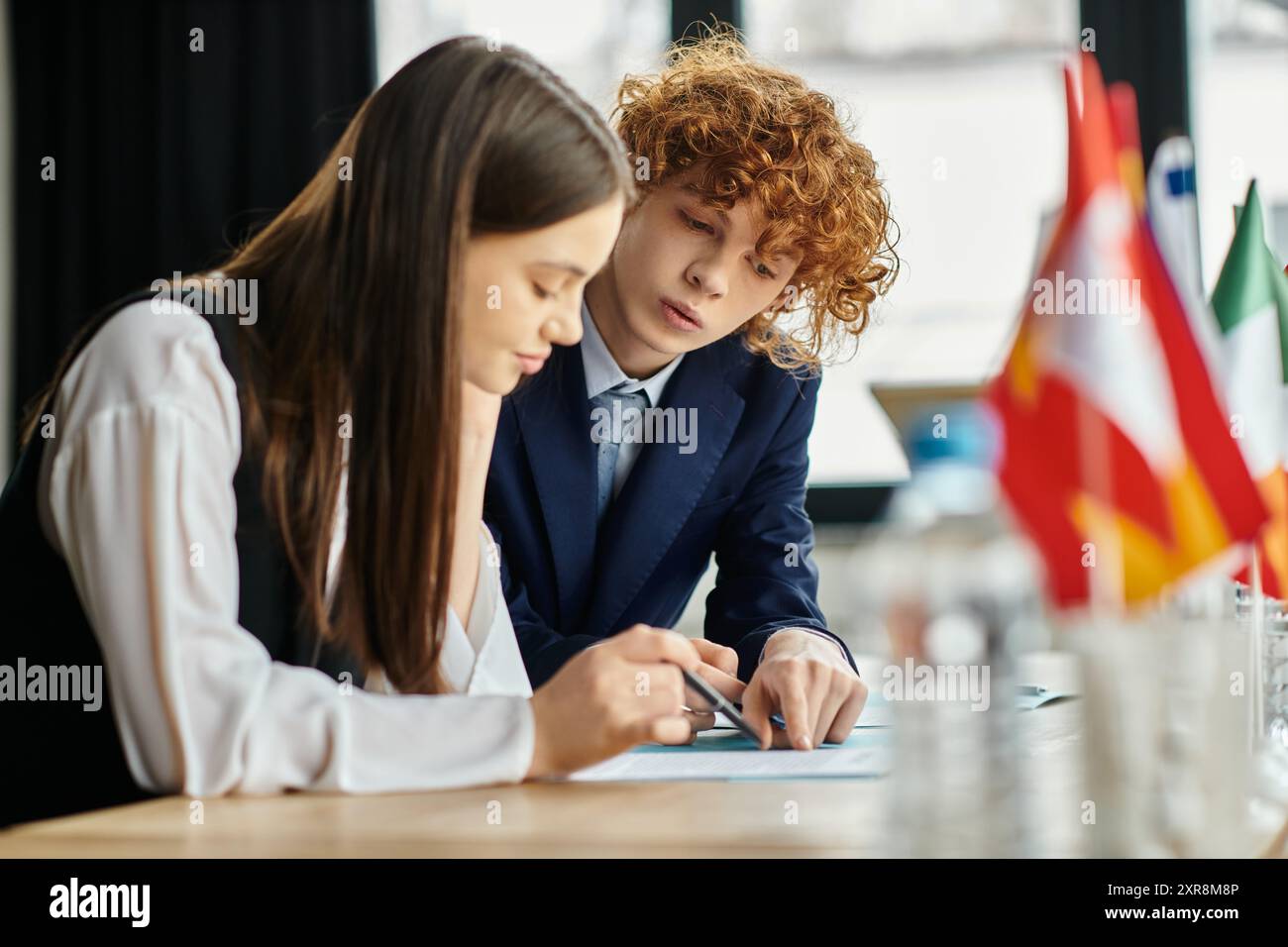 Two teenagers work together at a Model UN conference, surrounded by ...