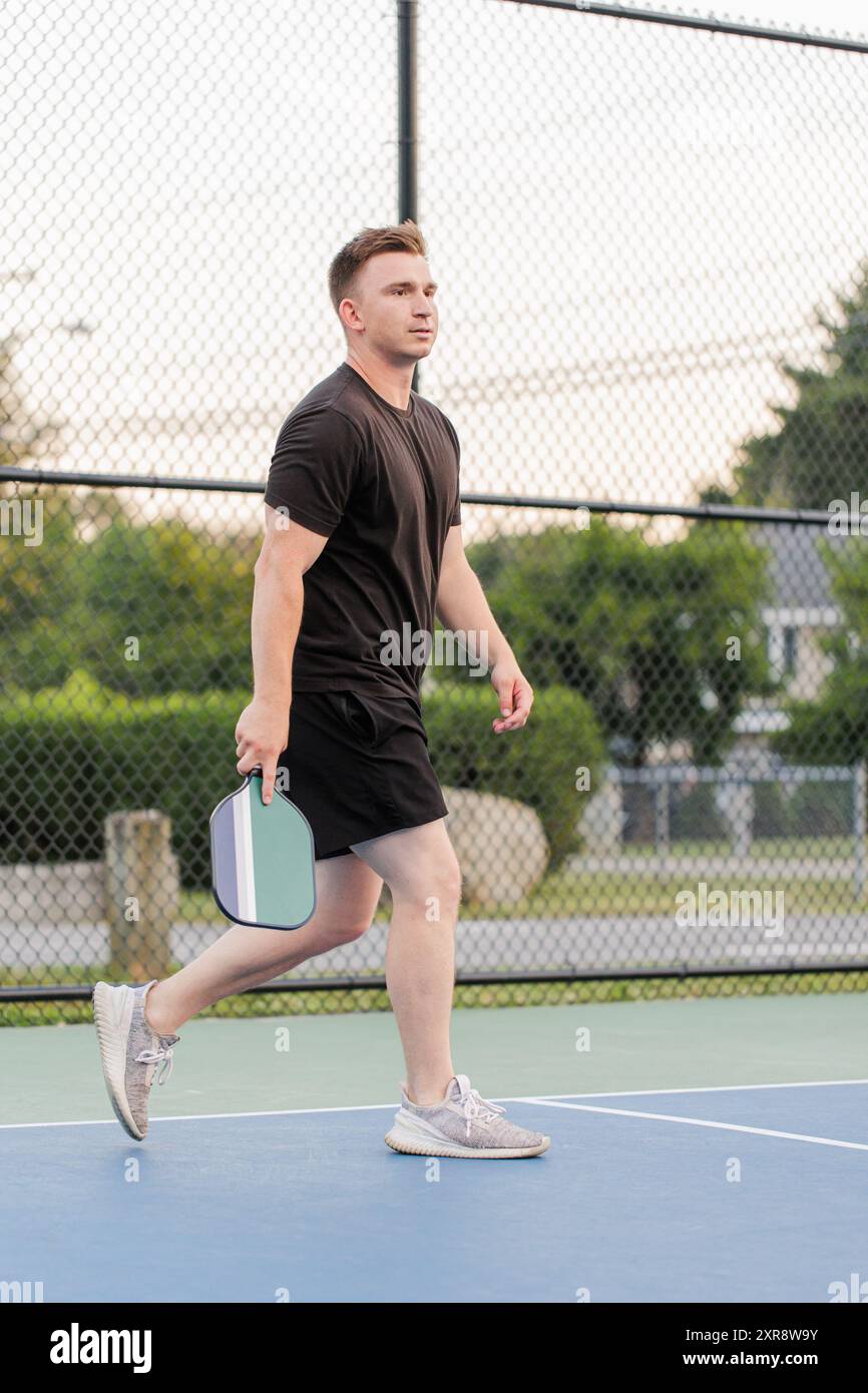 Young man walking on pickleball court holding a paddle Stock Photo - Alamy