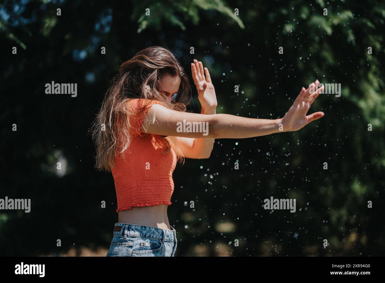Young woman shielding her face from water splash in the park on a sunny ...