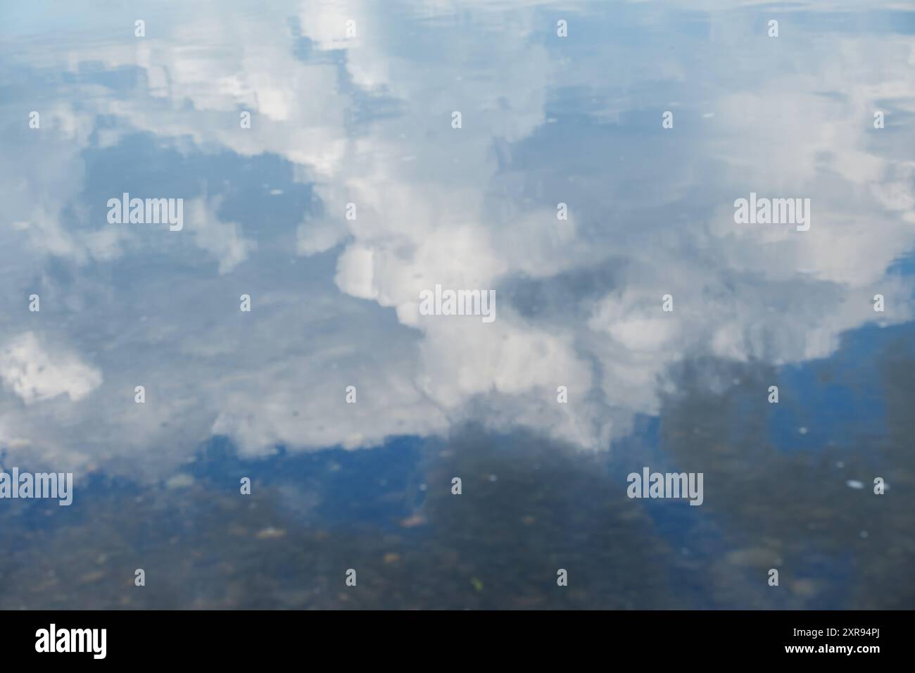 Reflection of sky and clouds on calm water surface creating serene ...