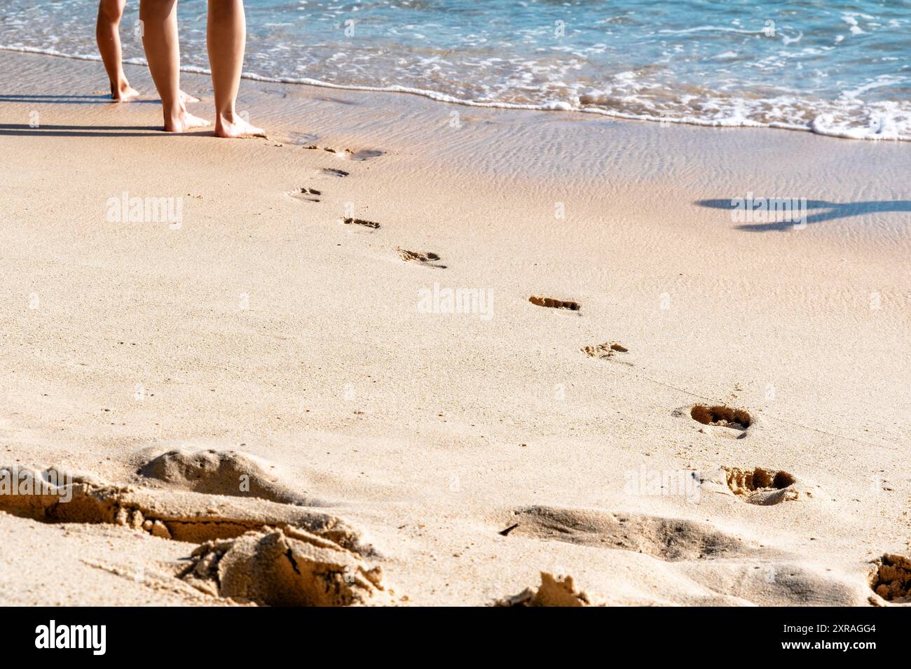 A close-up shot of footprints and human legs in the sand on a beach ...