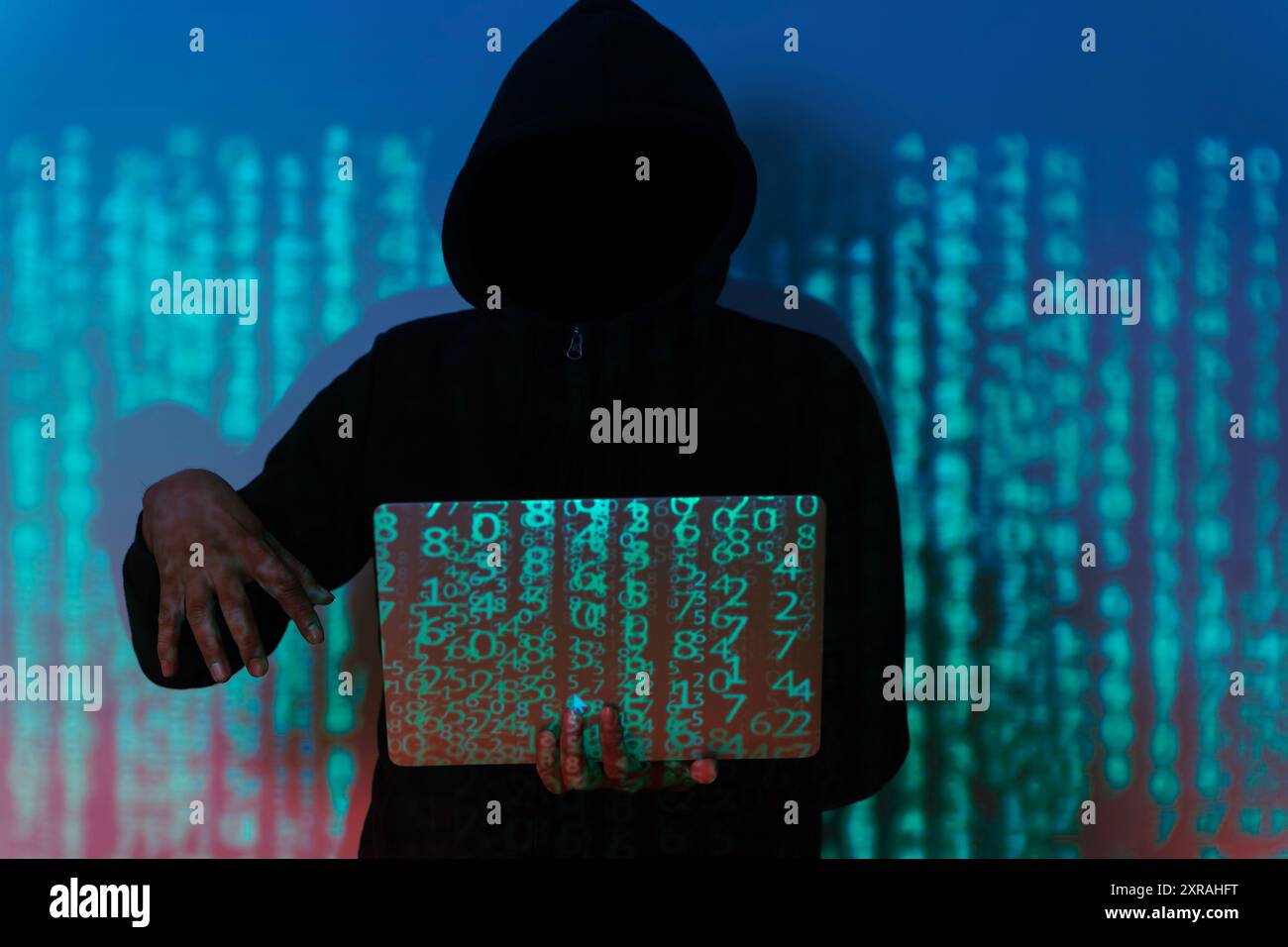 A hacker is sitting in a dark room, hunched over a laptop computer. The ...