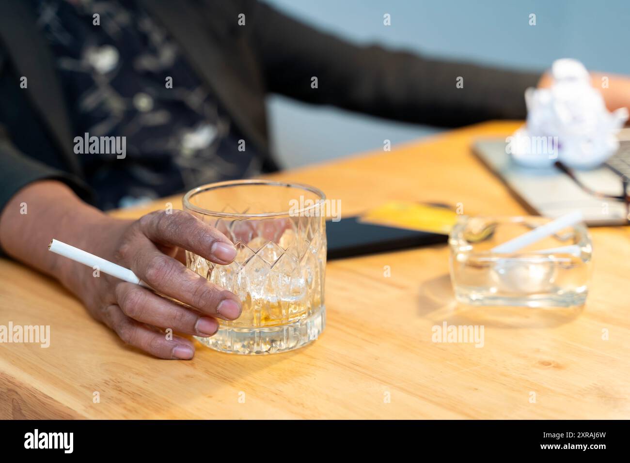 Close-up of a hand holding a glass of liquor. A disheveled man sits in ...
