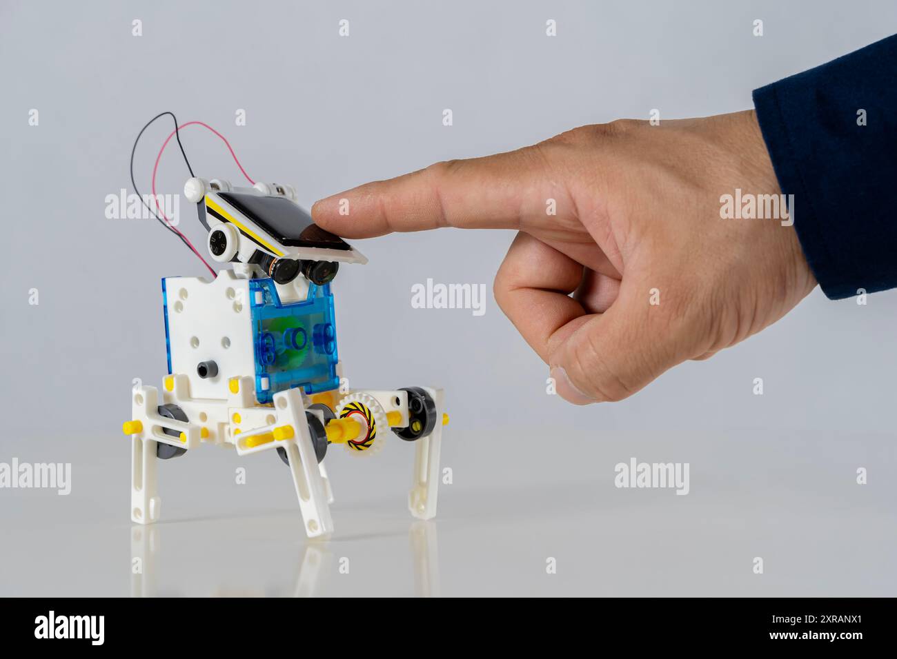 A finger touches a solar panel above a toy robot made from plastic ...