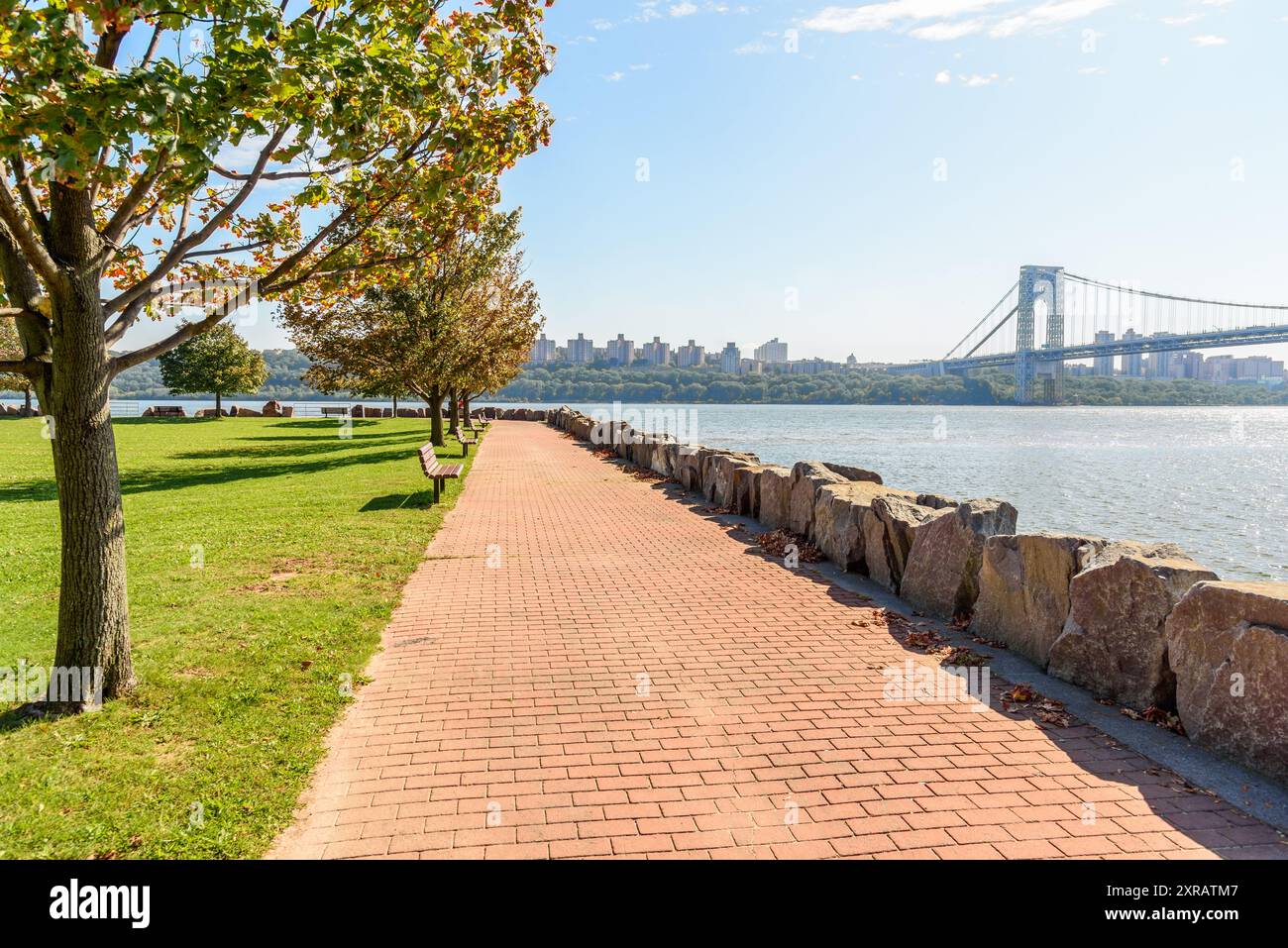 Brick riverside footpath lined with trees and benches on a sunny autumn ...