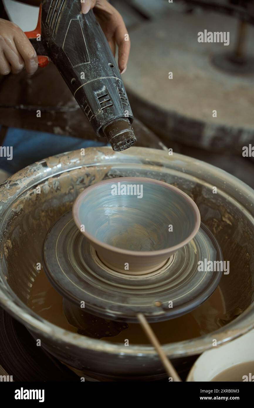 Expert potter drying earthenware bowl on pottery wheel using dryer tool ...