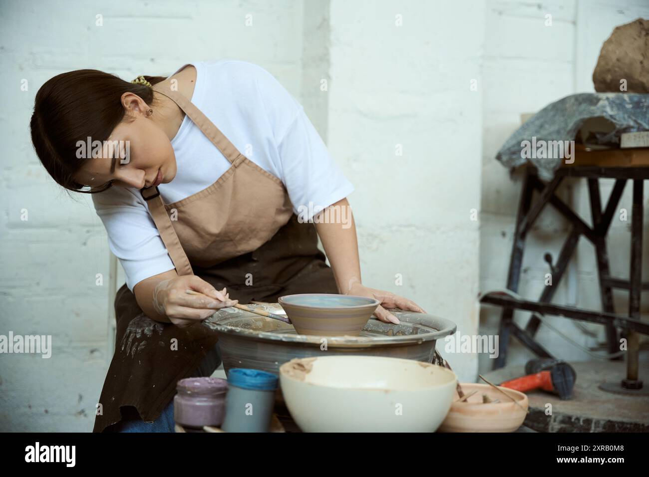 Focused female artist in apron making clay pottery on a spin wheel in ...