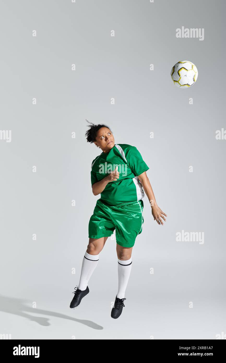 A female athlete in a green soccer uniform leaps to catch the ball mid ...