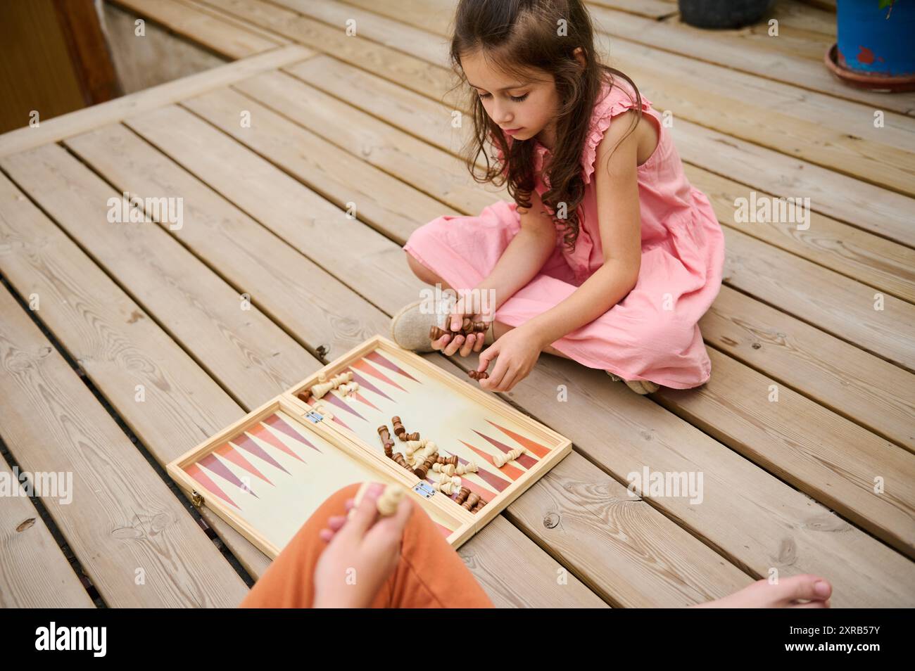 Young girl sitting on a wooden deck playing a game of backgammon. The ...