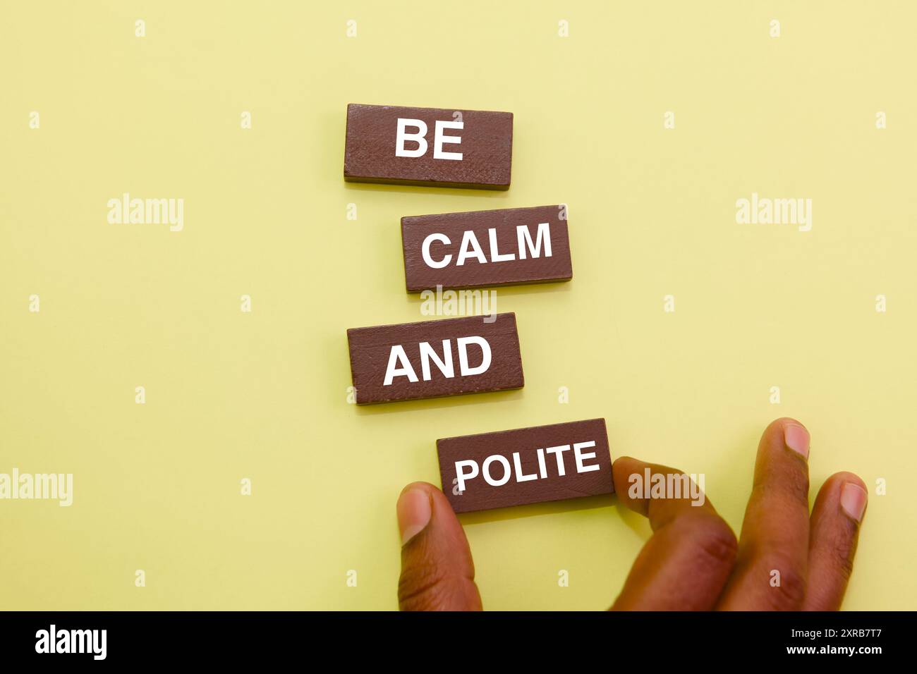 Hand arranging wooden blocks spelling "Be Calm and Polite" on a yellow ...