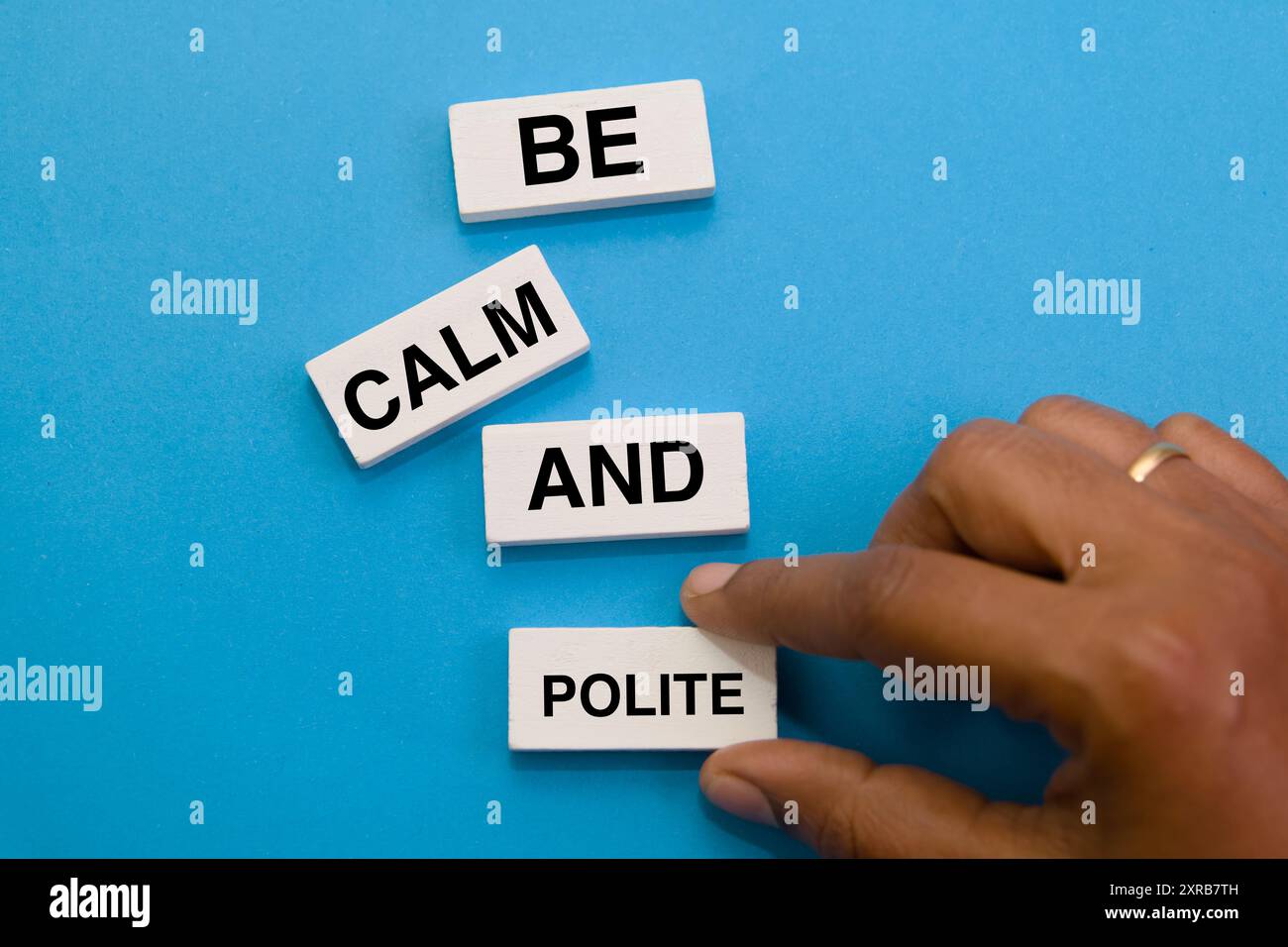 Hand placing wooden blocks spelling "Be Calm and Polite" on a vibrant ...