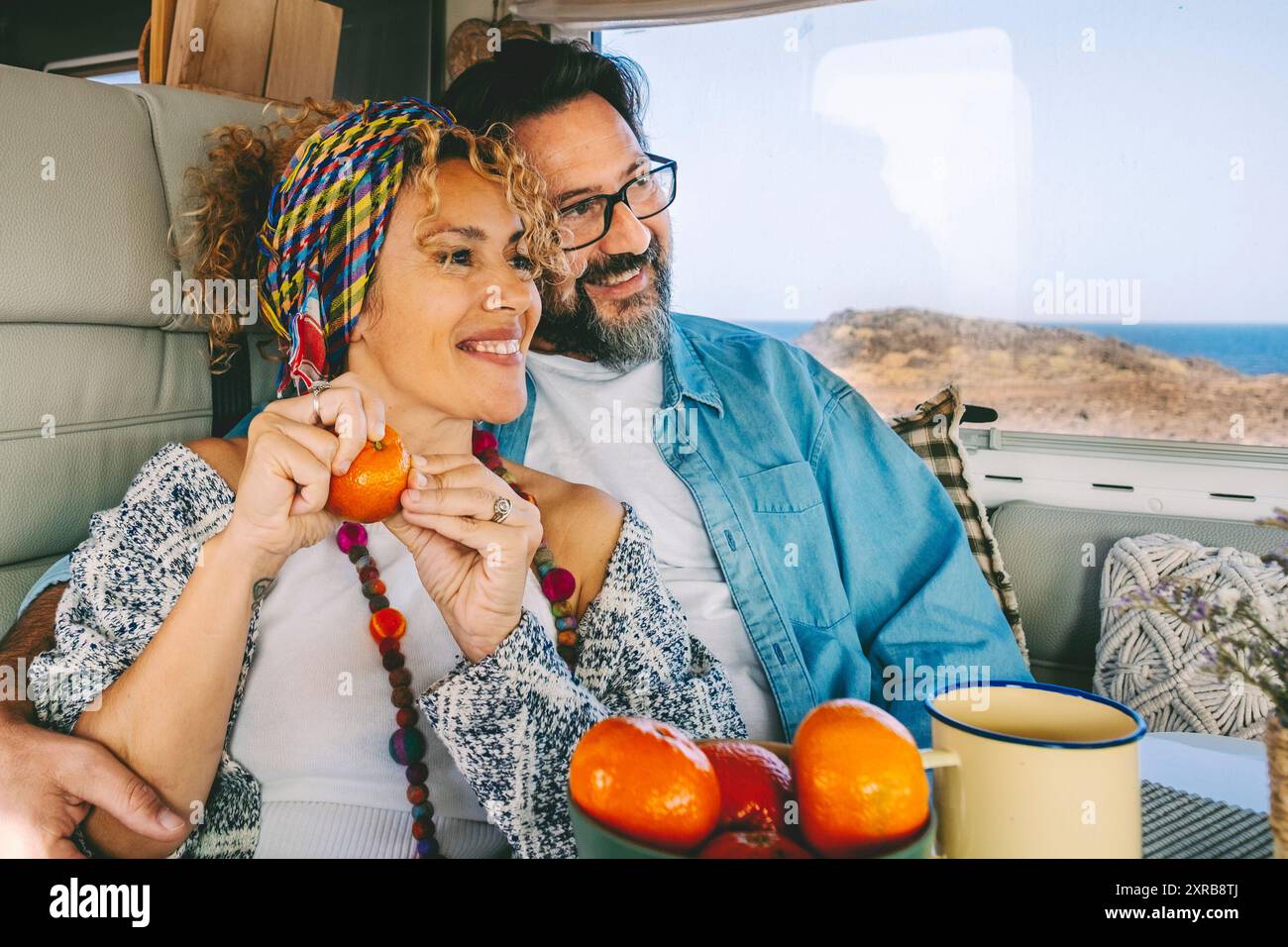Cheerful mature couple smile and hug sitting inside camper van and ...