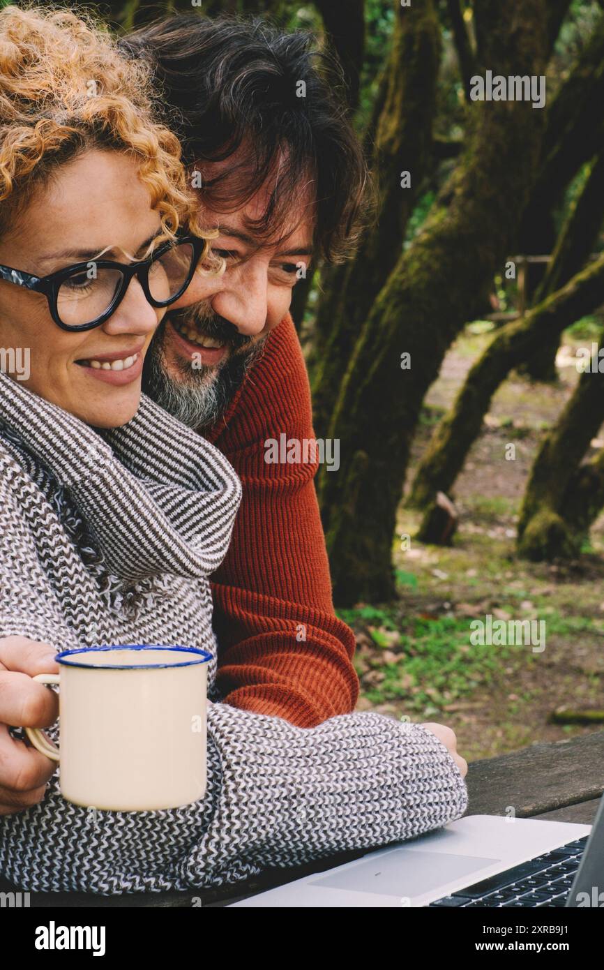 Man hugging woman while both using laptop in the outdoors nature park ...