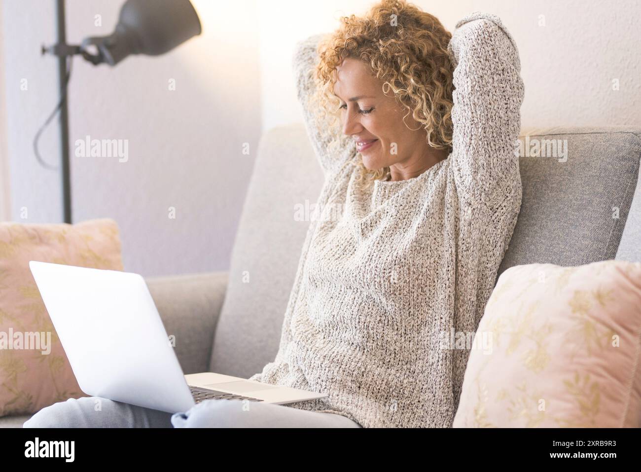 One cute adult woman using laptop sitting on the sofa in bright home ...