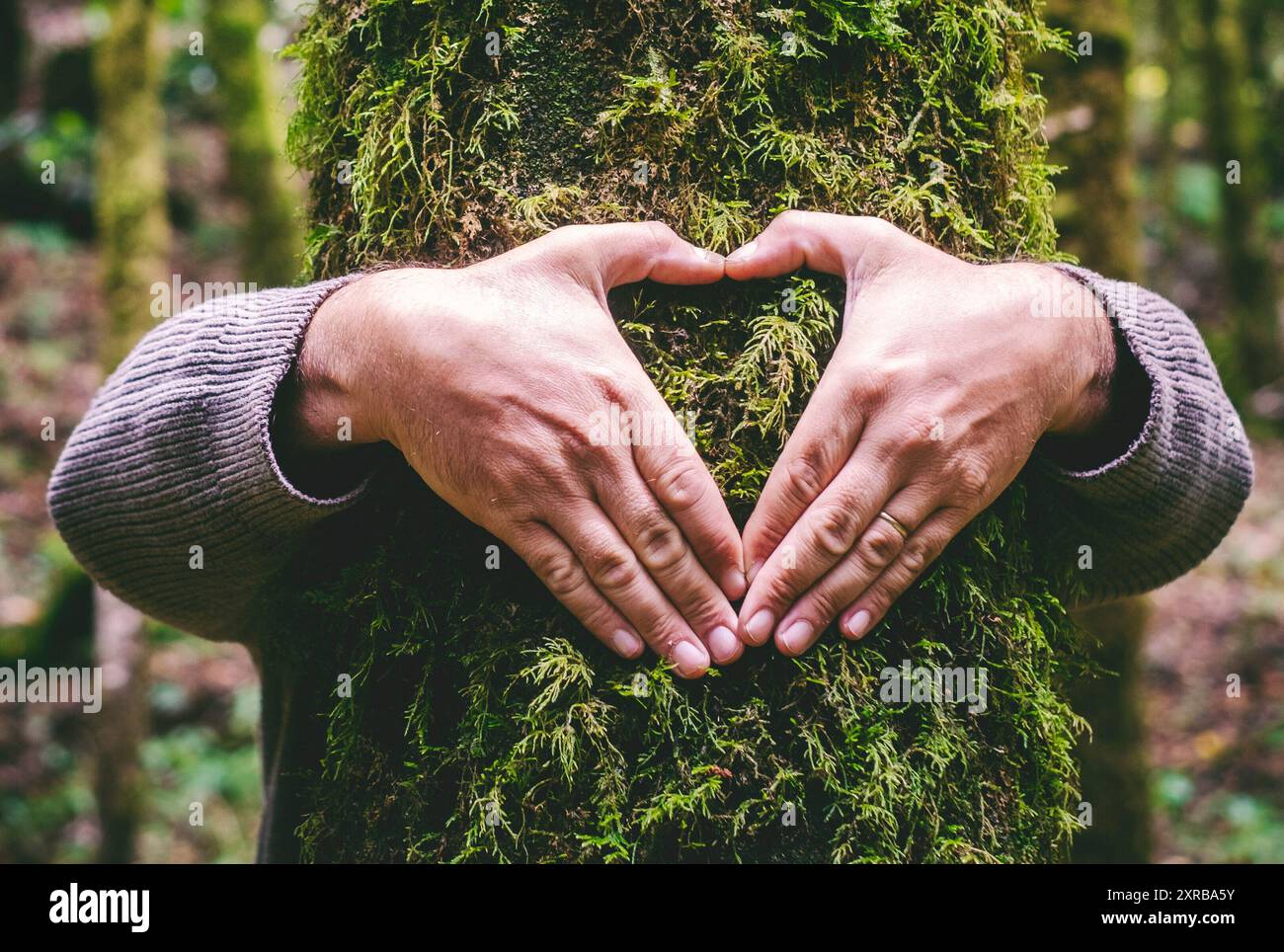 One man hugging a green tree trunk doing heart gesture with hands ...