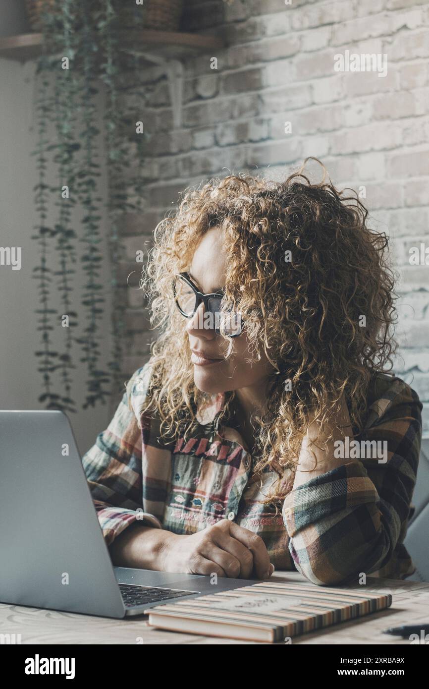 One adult woman using laptop at home with thoughtful expression looking ...