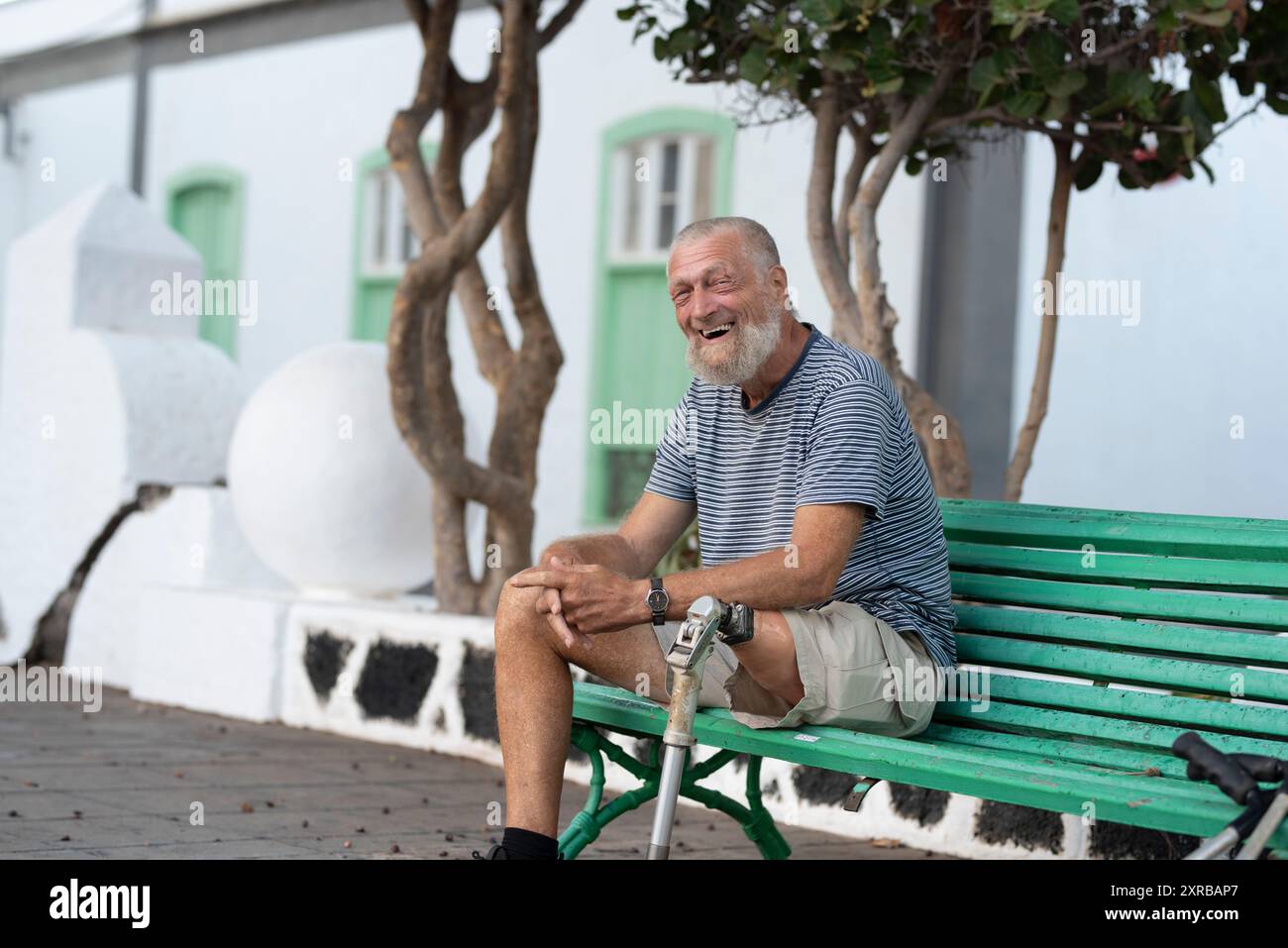 Elderly man with prosthetic leg left rests sitting on a park bench ...