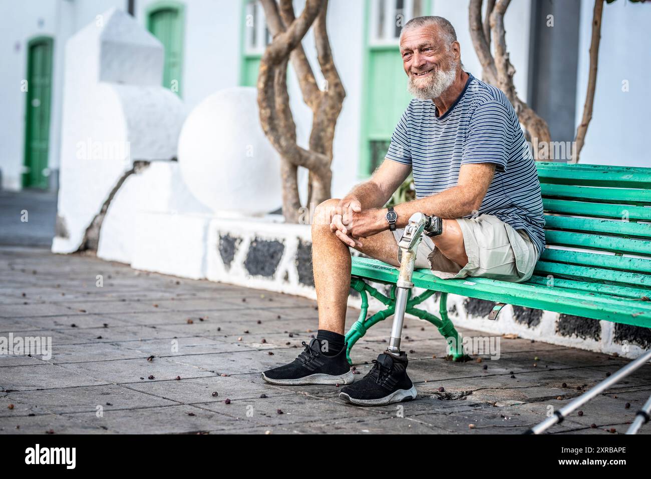 Elderly man with prosthetic leg left rests sitting on a park bench ...