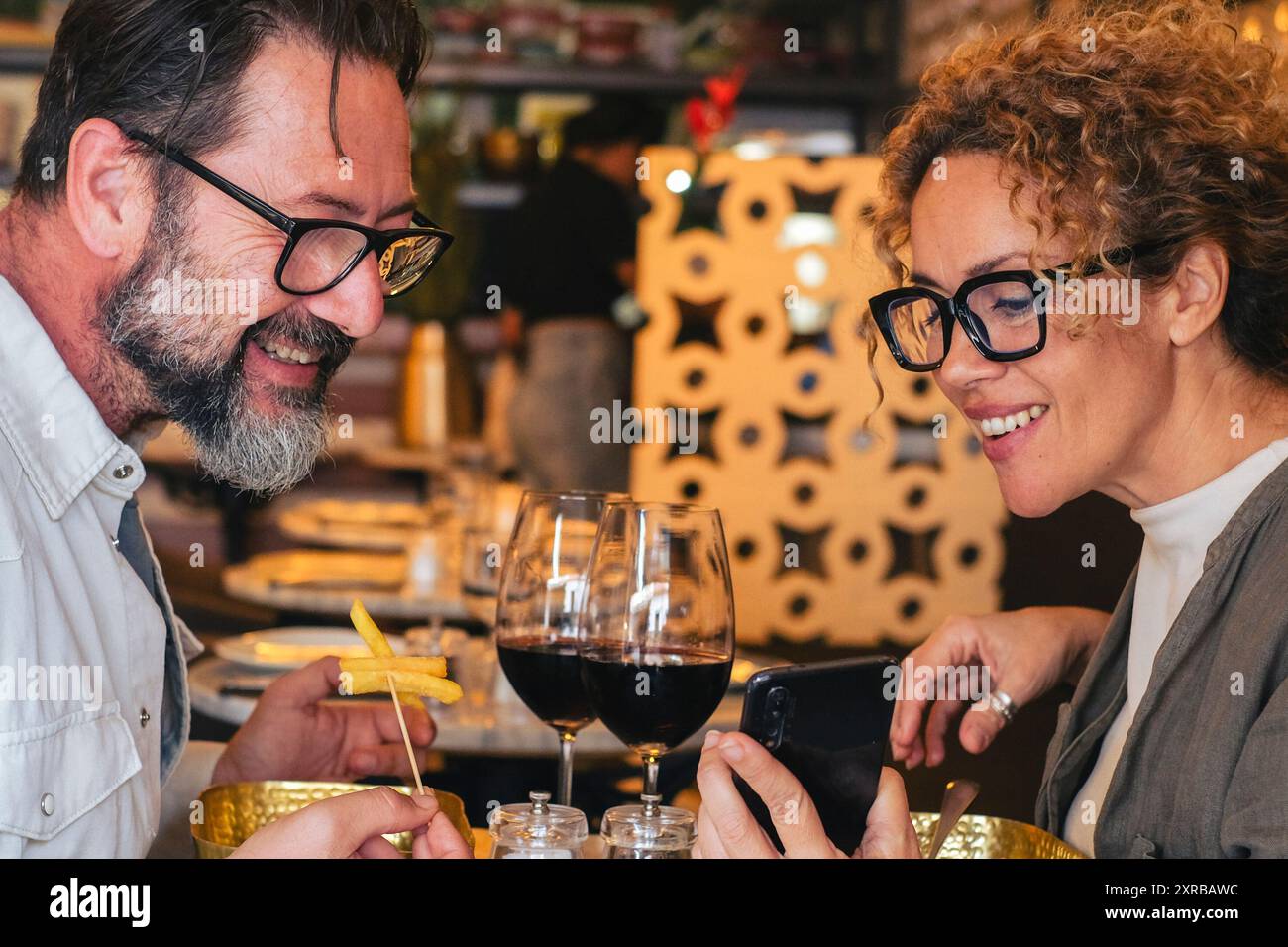 Happy couple smiling and talking in a restaurant looking at cell phone ...