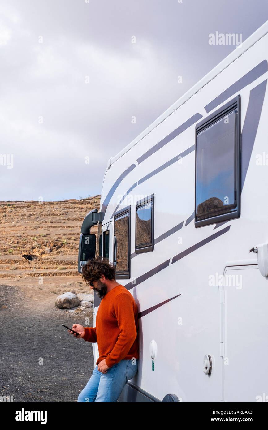 One traveler man using phone app outside a modern big camper van to ...