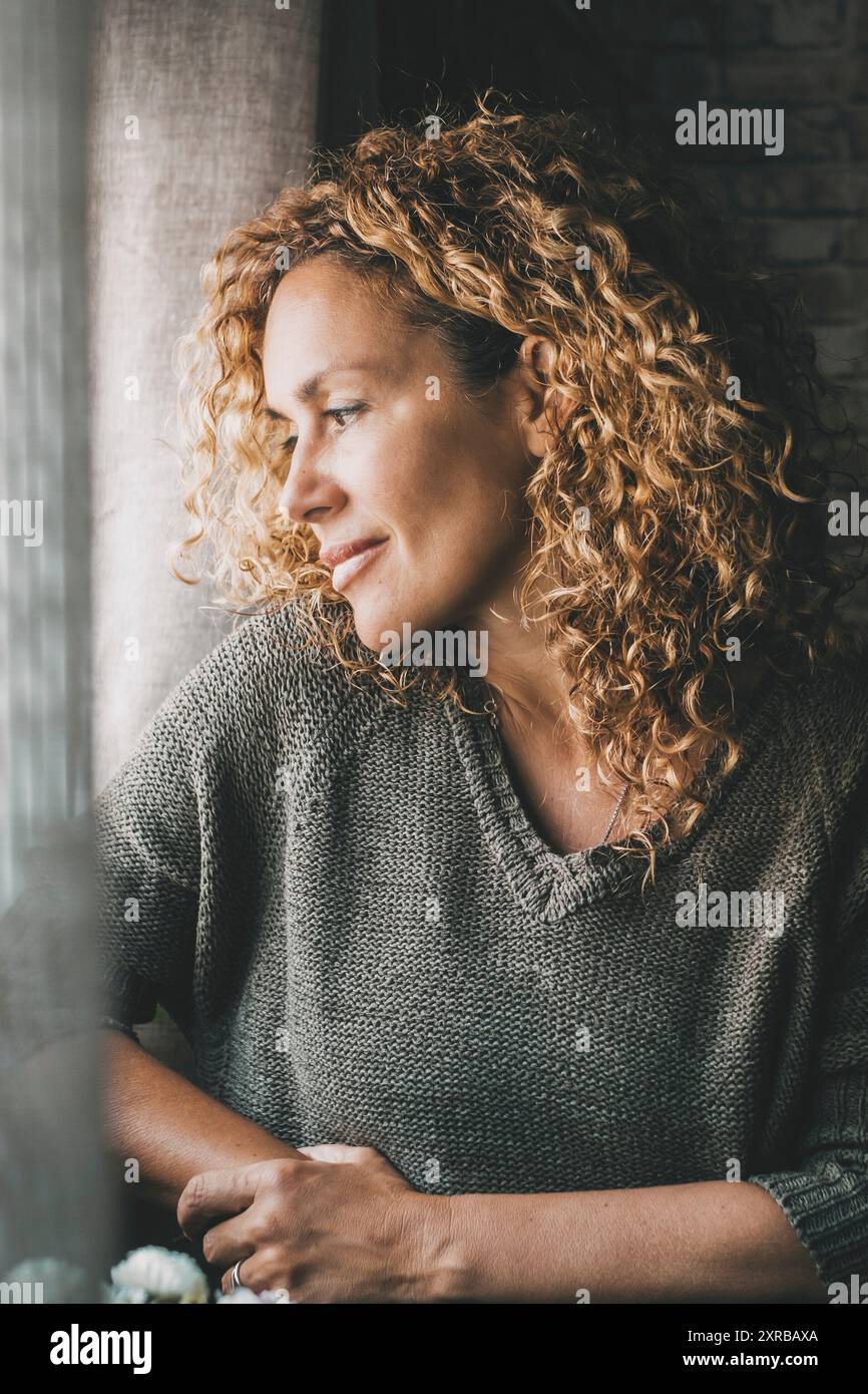 One serene adult woman looking outside the window at home with peaceful ...