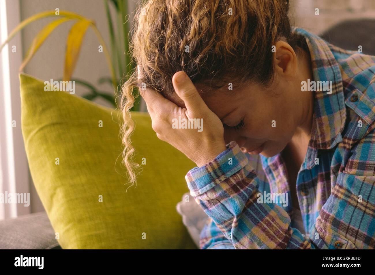 One exhausted and stressed woman at home sitting on the sofa touching ...