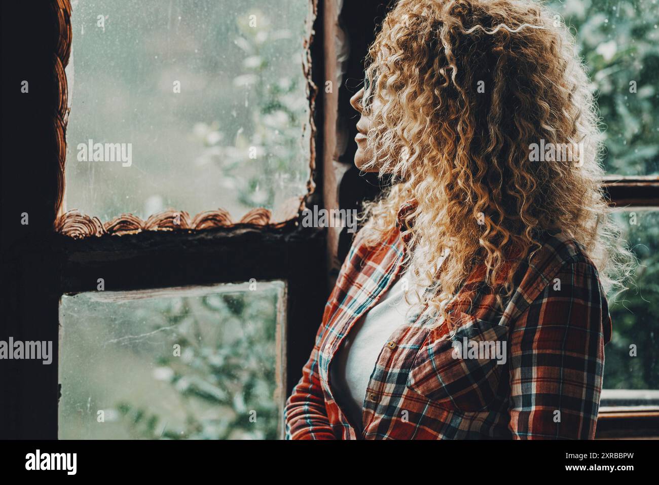 One woman standing alone at home looking outside the windows at nature ...