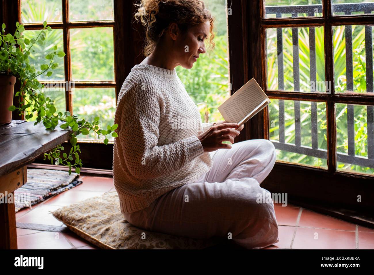 Serene woman reading a book at home sitting on the floor in total ...