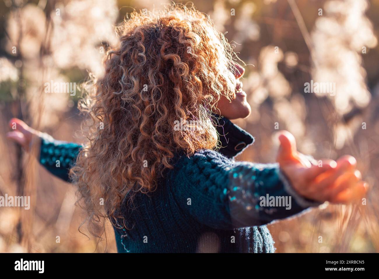 Back side view of woman enjoying sunset in golden field of grass ...