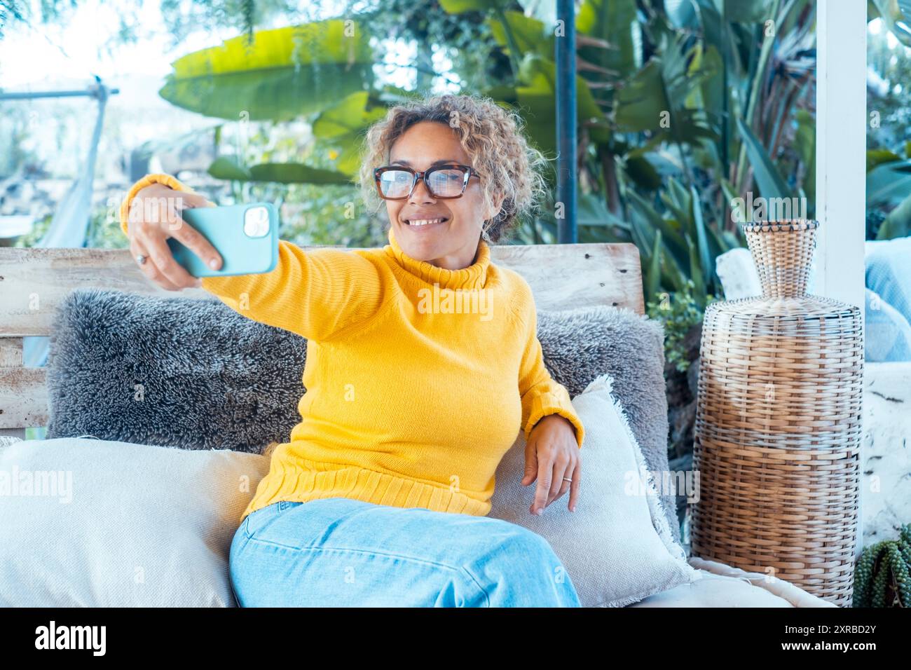 A woman uses her cell phone and relaxes alone in the garden sitting on ...