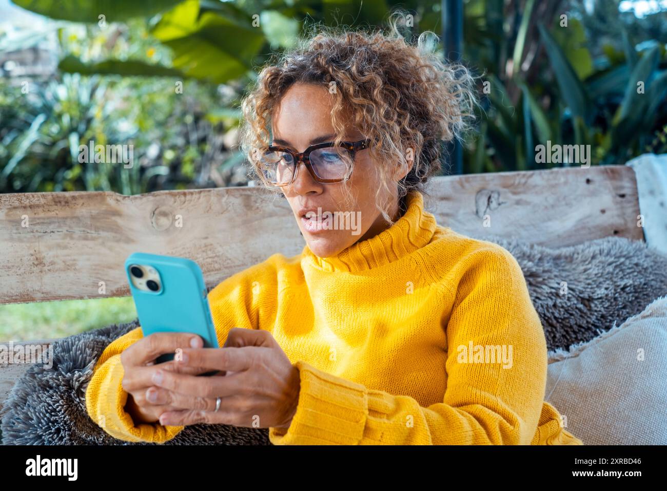 A woman uses her cell phone and relaxes alone in the garden sitting on ...