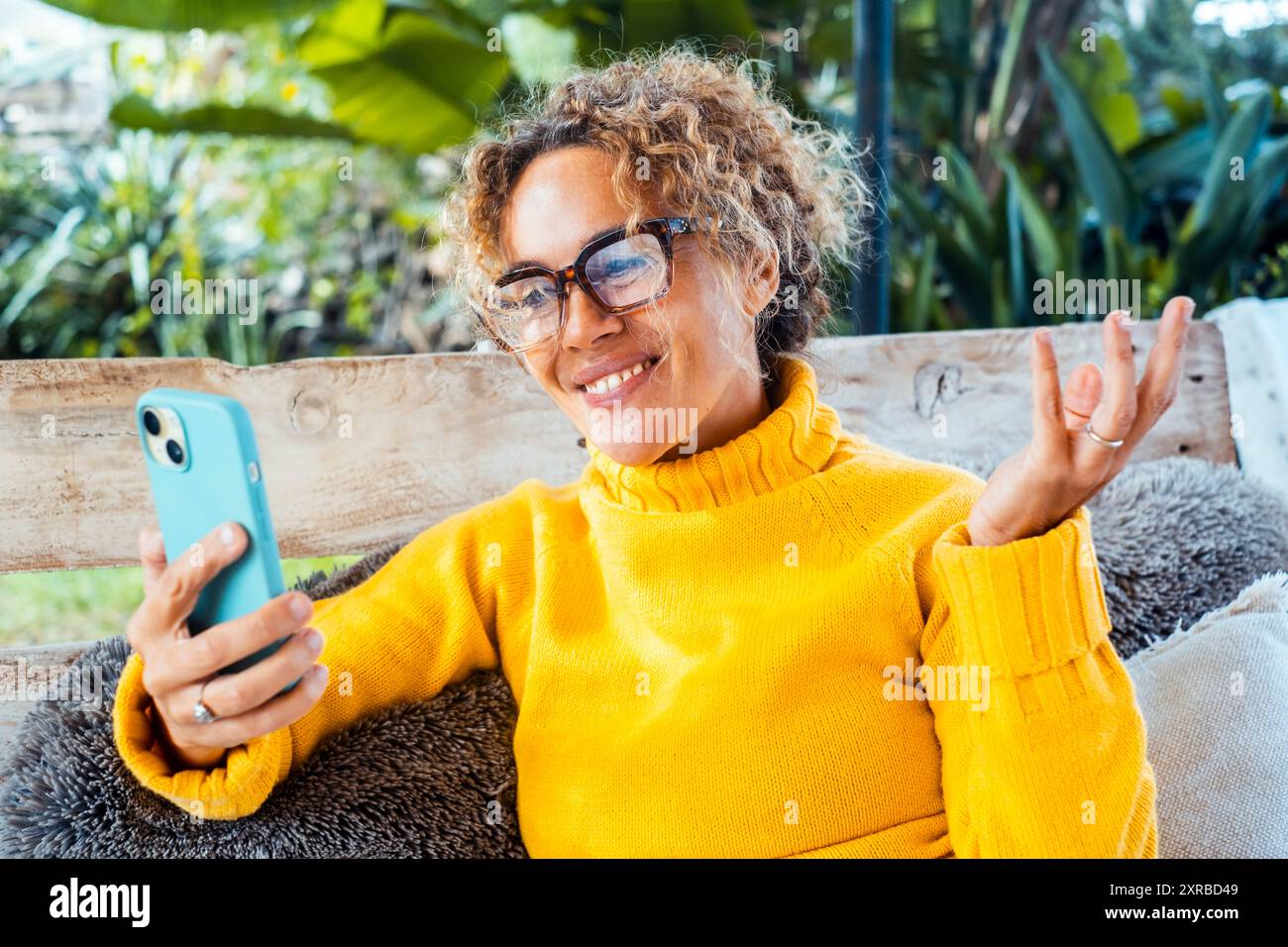 A woman uses her cell phone and relaxes alone in the garden sitting on ...