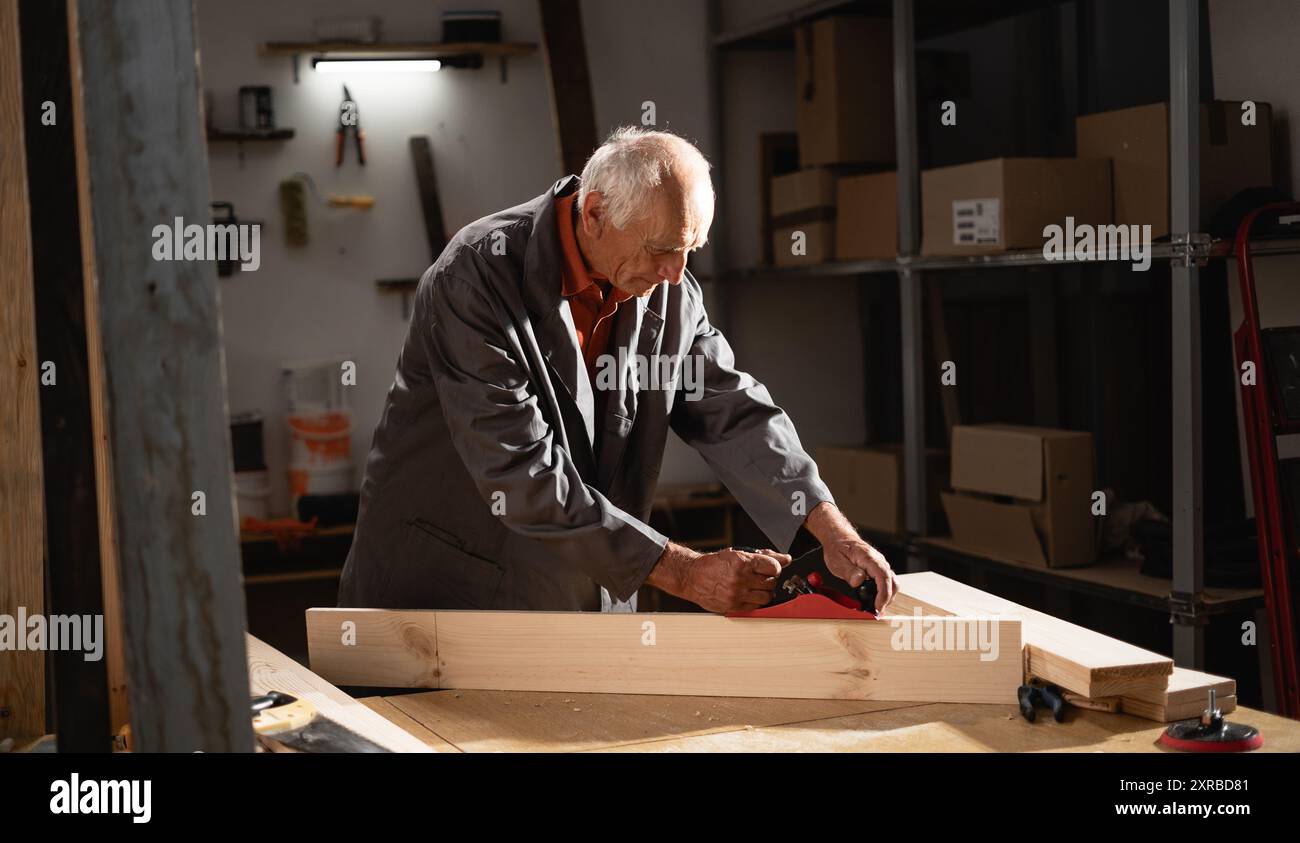mature carpenter planing plank while working in workshop enjoying ...