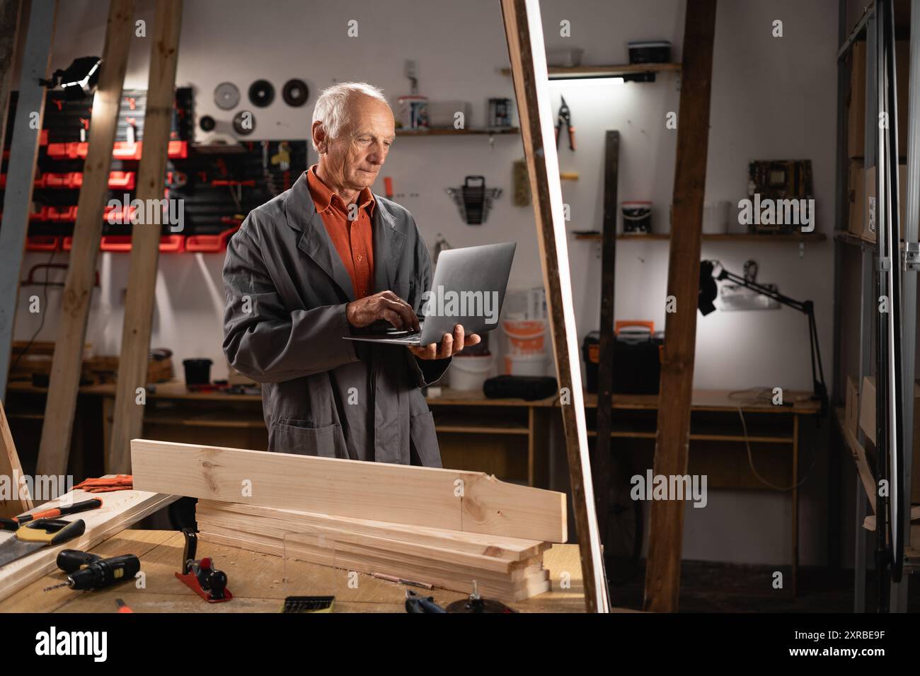 Carpenter using laptop computer standing in his carpentry workshop with ...